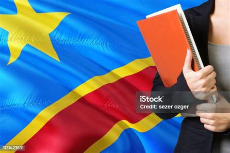Congolese 언어 개념을 학습 백그라운드에서 콩고 국기와 함께 서 있는 젊은 여자 책을 들고 교사 오렌지 빈 책 표지 교사