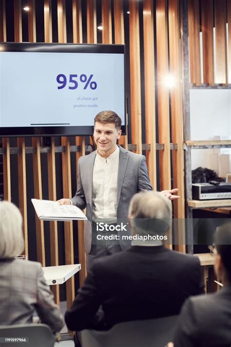 청중 앞에 서서 비즈니스 컨퍼런스에서 성공적인 마케팅 사례를 제시하는 정장에 자신감있는 젊은 사업가미소 경영자에 대한 스톡 사진