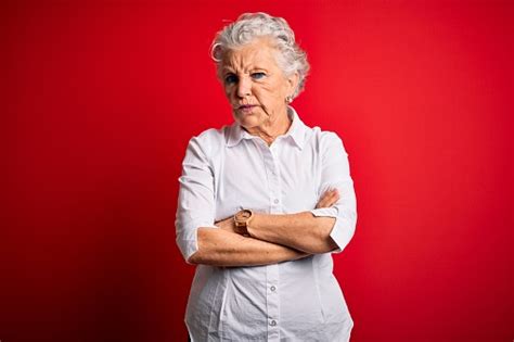 고립 된 빨간 배경 회의론자 와 긴장 교차 팔로 얼굴에 표정을 거부 위에 서 우아한 셔츠를 입고 선임 아름다운 여성 부정적인 사람 감정에 대한 스톡 사진 및 기타 이미지