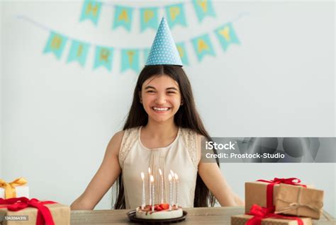 집에서 촛불이있는 선물 상자와 생일 케이크와 함께 테이블에 앉아있는 파티 모자에 쾌활한 인도 십대 소녀의 초상화 십대 소녀에 대한 스톡 사진 및 기타 이미지 Istock