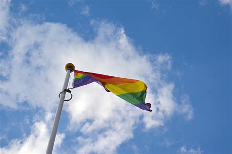 색상 레드 오렌지 노랑 녹색 파랑 및 보라 빛으로 무지개 깃발 게이 프라이드 플래그와 바람 푸른 하늘 구름 기둥에 달려있습니다