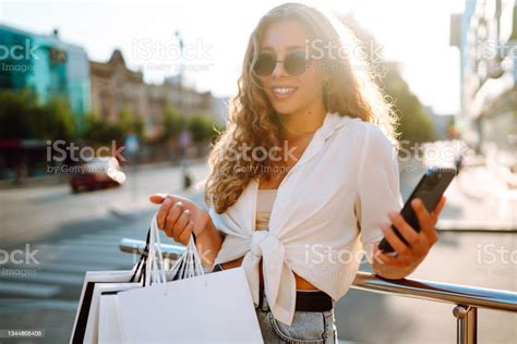 전화를 사용하고 쇼핑객 가방을 들고 야외에 서서 옷과 선물을 선택하고 주문하는 젊은 여성 가방에 대한 스톡 사진 및 기타 이미지 Istock
