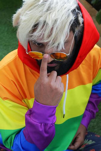 무지개 게이 Lgbt 플래그 후드를 입고 젊은 잘 생긴 힌두교 남자의 이미지 20대 초반 평화 표지판 짧은 수염 염색된 지저분한 금발 머리 손가락으로 선글라스를 들어 올리는