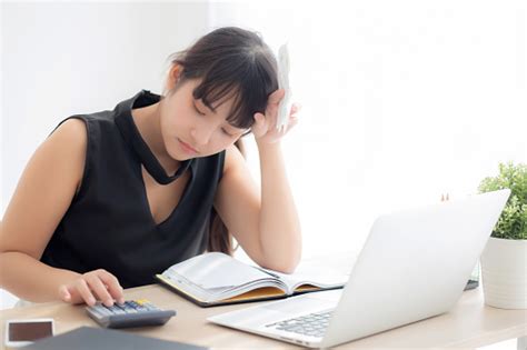 아름 다운 젊은 아시아 여성 계산 비용 가정용 및 쓰기 노트북 책상에 여자 법안과 스트레스를 확인 하 고 메모 여성 걱정 부채 및 세금 금융 및 비즈니스 개념 가정 생활에