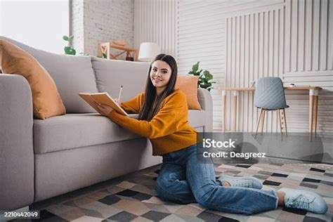 어린 소녀는 집 바닥에 앉아서 공책에 글을 쓰고 햇볕이 잘 들고 차분한 거실에서 세련된 실내 장식으로 둘러싸여 있습니다 16 17 살에 대한 스톡 사진 및 기타 이미지