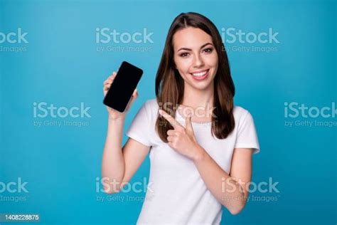 긍정적 인 소녀 프로모터의 사진 스마트 폰 포인트 검지 손가락 선택 선택 새로운 물체 제품 장치 착용 좋은 외모의 옷을 입고 고립 된 푸른 색 배경 보여주기에 대한 스톡