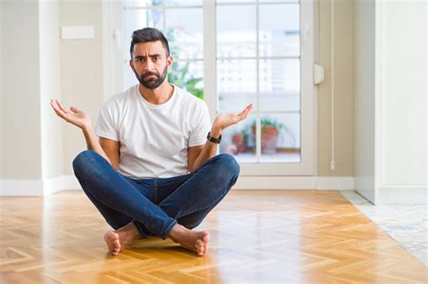 집에서 바닥에 앉아 캐주얼 티셔츠를 입고 잘 생긴 히스패닉 남자는 팔과 손을 들고 단서와 혼란 표정을 의심 개념 남자에 대한 스톡 사진 및 기타 이미지 Istock