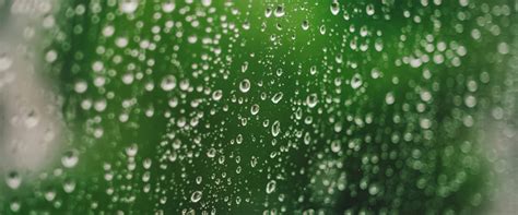 유리에 빗방울이 있는 대기 최소 배경 비오는 물방울과 먼지 얼룩이 있는 젖은 창문이 클로즈업됩니다 빗방울이 있는 더러운 창 유리에 녹지 보케가 있는 흐릿한 미니멀리스트 배경