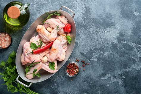 금속 팬 또는 어두운 회색 슬레이트 돌 또는 콘크리트 배경에서 요리하기위한 향신료와 재료와 그릇원시 닭 날개 검은 테이블에 향신료와 원시 고기 맨 위 보기입니다 모의