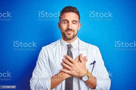 고립 된 배경 위에 흰색 전문 코트를 입은 젊은 잘 생긴 의사 남자는 닫힌 눈과 얼굴에 감사 제스처와 가슴에 손을 미소 건강