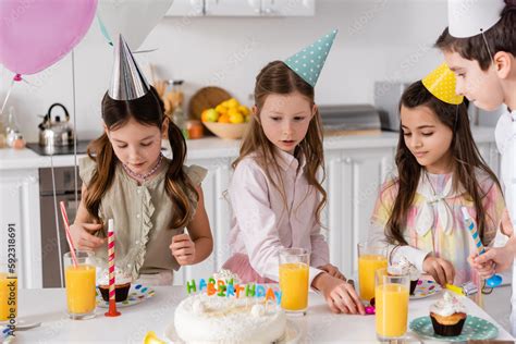 Preteen Girls In Party Caps Looking At Birthday Cake Next To Orange