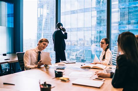 아프리카 계 미국인 남성 상사가 스마트 폰에서 사무실 인터넷 연결을 사용하여 기업 파트너에게 전화하면서 자신감있는 직원이 보고서 문서를 분석하고 공식적으로 옷을 입은 사업가