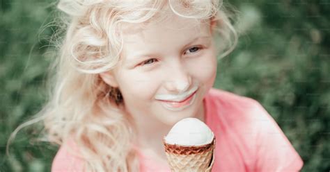 공원에 앉아 와플 콘에서 아이스크림을 핥는 긴 지저분한 금발 머리를 가진 귀여운 재미있는 사랑스러운 소녀 야외에서 맛있는 달콤하고 추운 여름 음식을 먹는 아이 여름 냉동