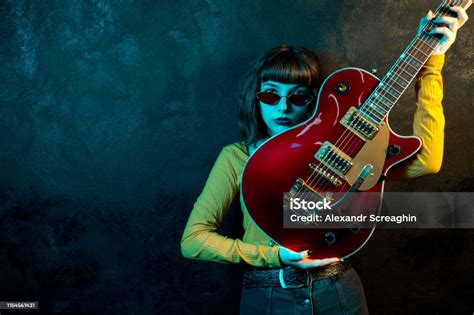 네온 불빛에 빨간 기타와 곱슬 머리를 가진 패션 젊은 소식통 여자 록 뮤지션은 일렉트릭 기타를 연주하 고 있습니다 90 년대