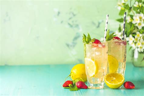 레몬과 딸기와 차가운 얼음 상쾌한 음료의 두 잔은 흰색 꽃이 피는 녹색 나무 테이블에 바 도구와 함께 제공됩니다 얼음 과일과 허브 장식으로 꾸며된 신선한 칵테일 음료 딸기에