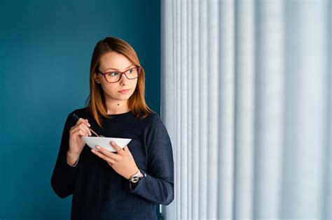 뮤즐리 또는 수프 식사와 함께 그릇을 들고 안경을 가진 젊은 여성은 집에서 창으로 먹는 숟가락이나 직장에서 쓰루 아침 식사