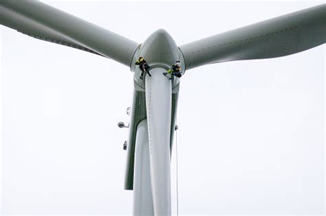 풍력 터빈의 바닥에서 볼 수 있으며 두 명의 로프 액세스 기술자 로프의 블레이드허브에서 아래로 내려오는 산업 등반가 검사 및 블레이드 수리 풍력발전기에 대한 스톡 사진 및