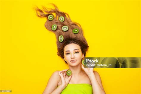 긴 머리 사람 및 음식에 키위 과일 조각과 색깔의 배경에 누워 아름다운 소녀의 패션 초상화 젊은 평화로운 여자는 아름다움과 몸을 돌봅니다 가리기에 대한 스톡 사진 및 기타