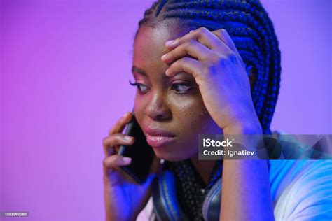보라색 배경이있는 녹음 스튜디오에서 휴대 전화로 그녀의 목에 헤드셋을 가진 화가 젊은 아프리카 여성 우리는 클로즈업에서 그녀를 참조하십시오 스튜디오에 대한 스톡 사진 및