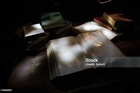 반짝이는 황금색 배경이 있는 나무 탁자 위에 열린 고대 책의 그림책을 상상해 보십시오 마법의 힘으로 마법 빛나는 책 주위 번개 어둠의 방에서 0명에 대한 스톡 사진 및 기타