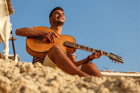 바위가 많은 해변에 앉아 어쿠스틱 기타를 연주하는 즐거운 청년의 전체 길이 샷 기타 현악기에 대한 스톡 사진 및 기타 이미지 기타 현악기 청년 남자 해변 Istock