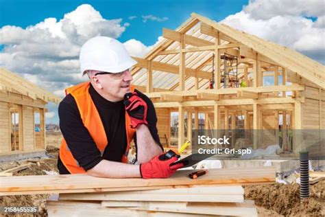 남자 건축 목조 건물 보드에서 주택 건설 프레임 건물 건설 건축업자 제복을 입은 남자가 줄자를 들고 있다 가이는 시골 별장을 디자인합니다 헬멧을 쓴 건축가 45 49세에