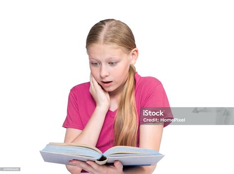놀란 소녀는 책을 읽고 손으로 뺨을 만지고 흰색 배경에 고립되어 있습니다 분홍색 티셔츠를 입은 금발 아이 표정이 풍부한 얼굴 감정적 인 반응 T 셔츠에 대한 스톡 사진 및