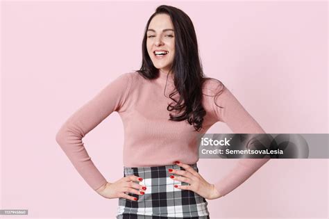 사랑 스러운 어두운 머리 소녀에 장미 셔츠 Nad 체크 스커트 카메라를 보면서 웃 고 엉덩이에 손으로 포즈 재미 있는 농담을 듣고 당신의 Edvertisment 공간을 복사