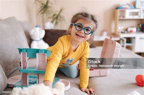 사랑스러운 어린 소녀는 미소를 짓고 그녀의 방에서 의사를 연기합니다 귀여운 세 살짜리 소녀는 놀면서 시간을 보냅니다 안경 노란색 블라우스와 파란색 레깅스를 착용 한 소녀