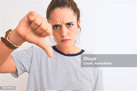 화가 난 얼굴로 고립 된 배경 위에 빵을 입고 있는 젊은 빨간 머리 현대 여성 엄지 손가락으로 싫어하는 것을 보여주는 부정적인 표지판 거부 개념 분노에 대한 스톡 사진 및