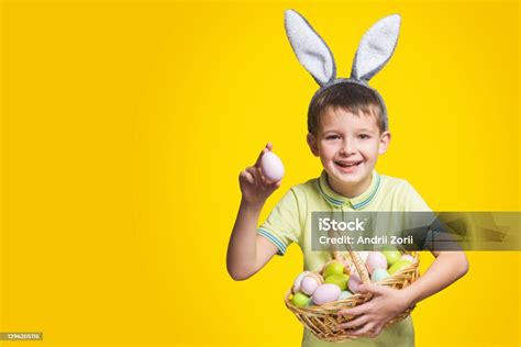 부활절 토끼 귀를 쓰고 행복한 스밀링 소년이 노란 배경에 그려진 달걀바구니를 들고 있다 공간을 복사합니다 부활절 날 검색에 대한 스톡 사진 및 기타 이미지 Istock