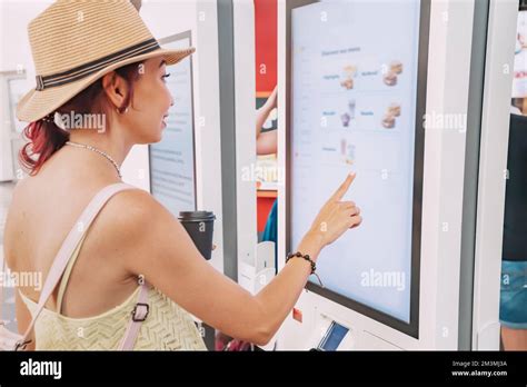 A Female Customer Uses A Touchscreen Terminal Or Self Service Kiosk To Order At A Fast Food