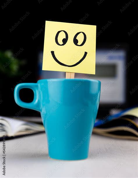 Smiling Face Drawn On Sticky Note Inside A Cup Of Coffee At The Office