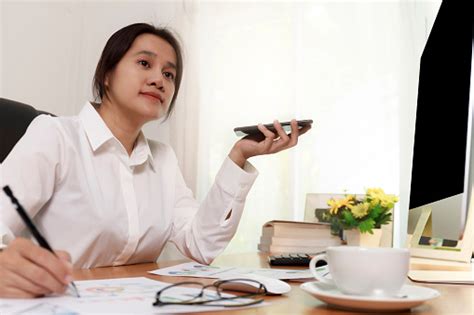 스마트 폰을 들고 스피커 폰으로 말하고 사무실에서 책상에 메모를 작성하는 비즈니스 여성 비즈니스 사람들은 고객 또는 스마트 폰