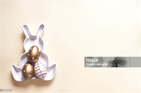 현대적이고 금색의 부활절 달걀은 복사 공간이있는 파스텔 노란색 배경에 부활절 토끼 형태로 접시에 있습니다 행복한 부활절 가로 배너 템플릿입니다 0명에 대한 스톡 사진 및