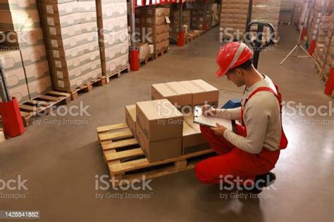Worker Holding Clipboard Near Pallet With Boxes In Warehouse Stock