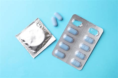 Pílulas e preservativos em fundo azul claro problema de potência Foto