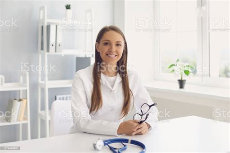 진료소 사무실에서 직장에 앉아있는 동안 카메라 화상 통화를보고 미소 여성 의사 의료직에 대한 스톡 사진 및 기타 이미지 의료직 책상 30 34세 Istock