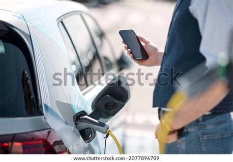 젊은 남자가 충전소에서 전기자동차가 충전되는 동안 스톡 사진 2077896709 Shutterstock