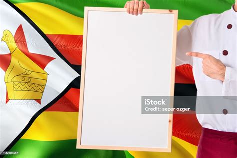 짐바브웨 국기 배경에 빈 화이트 보드 메뉴를 들고 짐바브웨 요리사 텍스트에 대 한 균일 한 포인팅 공간을 착용 요리 고급 요리에 대한 스톡 사진 및 기타 이미지 Istock
