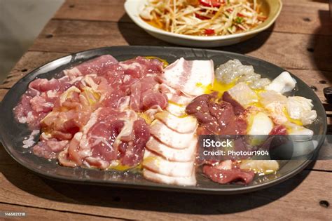 스키야키샤브야키니쿠 그릴을 위한 고기 세트는 나무 테이블 위에 놓인 검은 접시에 담겨 있습니다 생고기 세트에는 쇠고기 돼지 고기 베이컨 간 생선 오징어 새우가 포함됩니다 간