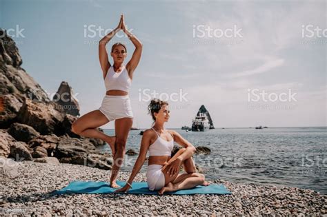 여자 바다 요가 요가에서 명상하는 두 명의 행복한 여성이 해변 바다 바위 산에서 포즈를 취합니다 동기 부여와 영감을주는 적합과 운동 자연 속에서 야외에서 건강한 라이프스타일