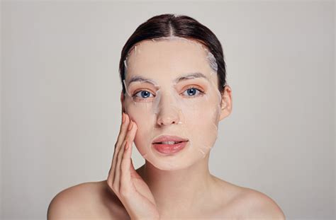 그녀의 얼굴을 만지고 보습 얼굴 마스크와 푸른 눈과 전체 입술을 가진 젊은 아름다운 포만기 소녀 회색 배경입니다 어두운 머리 기대 공간을 복사합니다 건강한 생활방식에 대한