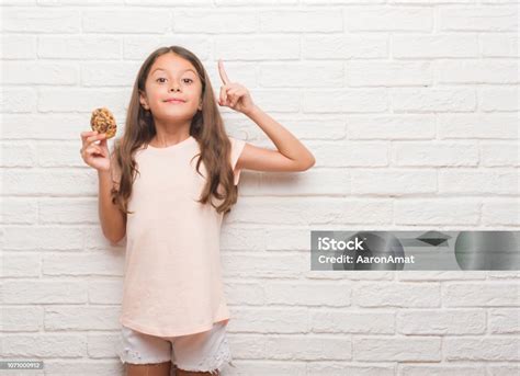 흰색 벽돌 벽 먹는 초콜릿에 젊은 히스패닉 아이 칩 쿠키 생각이 나 질문 넘버 원 행복 한 얼굴로 손가락을 가리키는 놀된