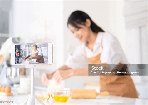 라이브 스트림에서 베이킹하는 과정을 보여주는 집중된 젊은 여성 음식 블로거의 초상화 삼각대에 스마트폰 앞에 서 방송 부엌 배경에서 촬영한 실내 스튜디오입니다 25 29세에