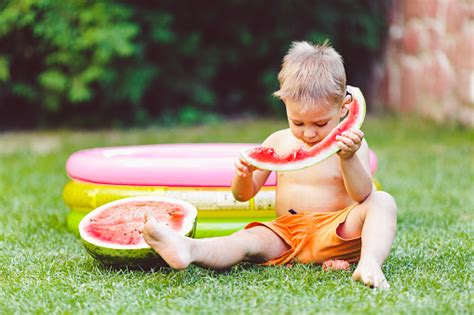 테마 여름 제철 음식 육즙 수박 베리 작은 재미 백인 소년 아이 2 년 뒤뜰 녹색 잔디 잔디와 먹는 조각 수박 손을 잡고 앉아 벌거 벗은 에 반바지 과 맨발 공기 주입에