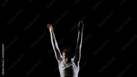 Young Handsome Male Acrobat Gymnast In White Clothes On A Black