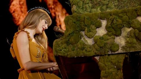 A Woman In A Yellow Dress Standing Next To A Moss Covered Wall And