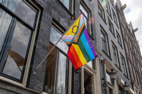 Progress Pride Flag With Intersex Symbol Displayed On A Building Facade In An Urban Street
