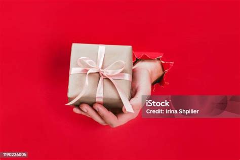빨간 배경의 구멍을 통해 분홍색 리본공예 종이에 싸여 선물 상자를 들고 남성 손 2020년에 대한 스톡 사진 및 기타 이미지 2020년 개념 겨울 Istock